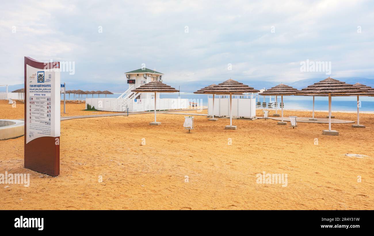 Ein Bokek, Israel - January 22, 2020: Empty Dead Sea sandy beach with sun umbrellas and info ...