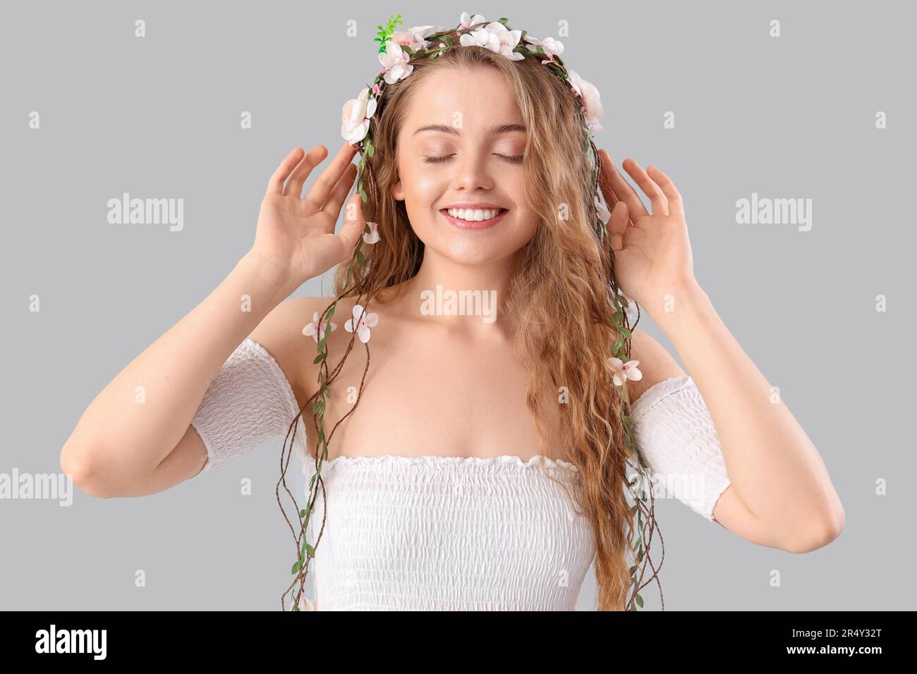 Beautiful young woman with flowers in her hair on light background ...