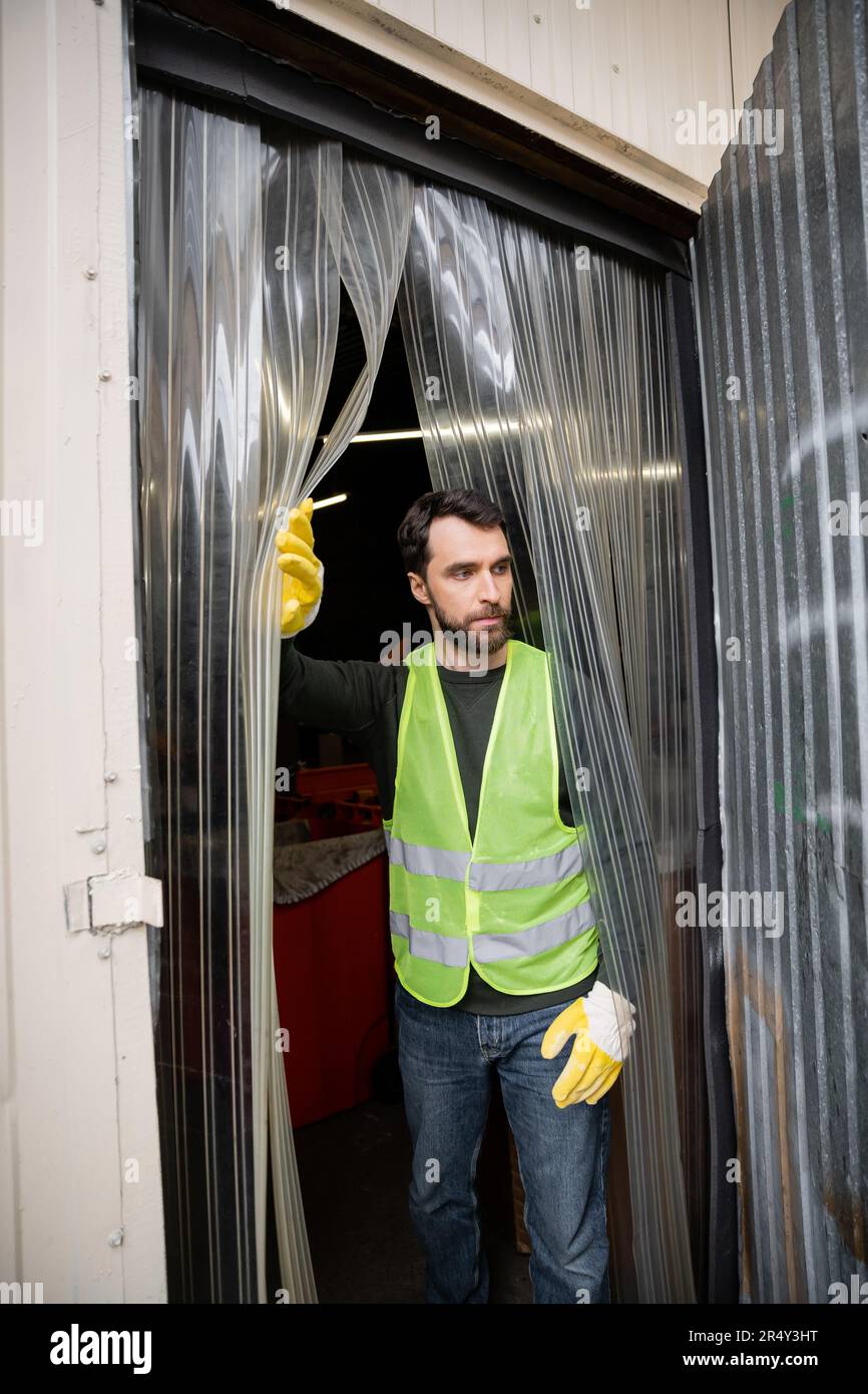 Bearded male worker in high visibility vest and gloves standing near ...