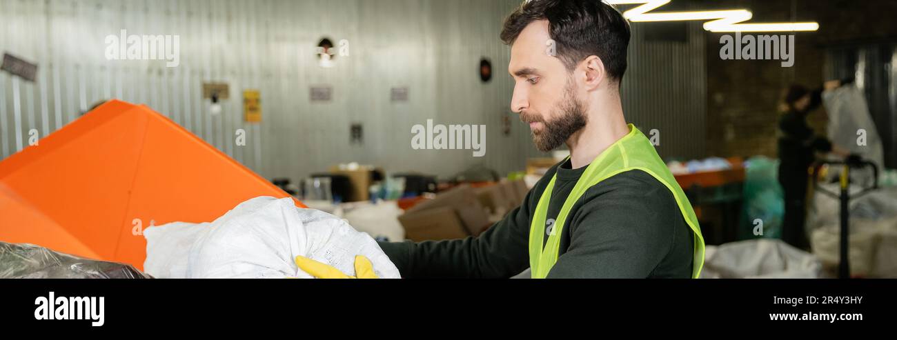 Side view of bearded sorter in protective vest and glove putting trash ...
