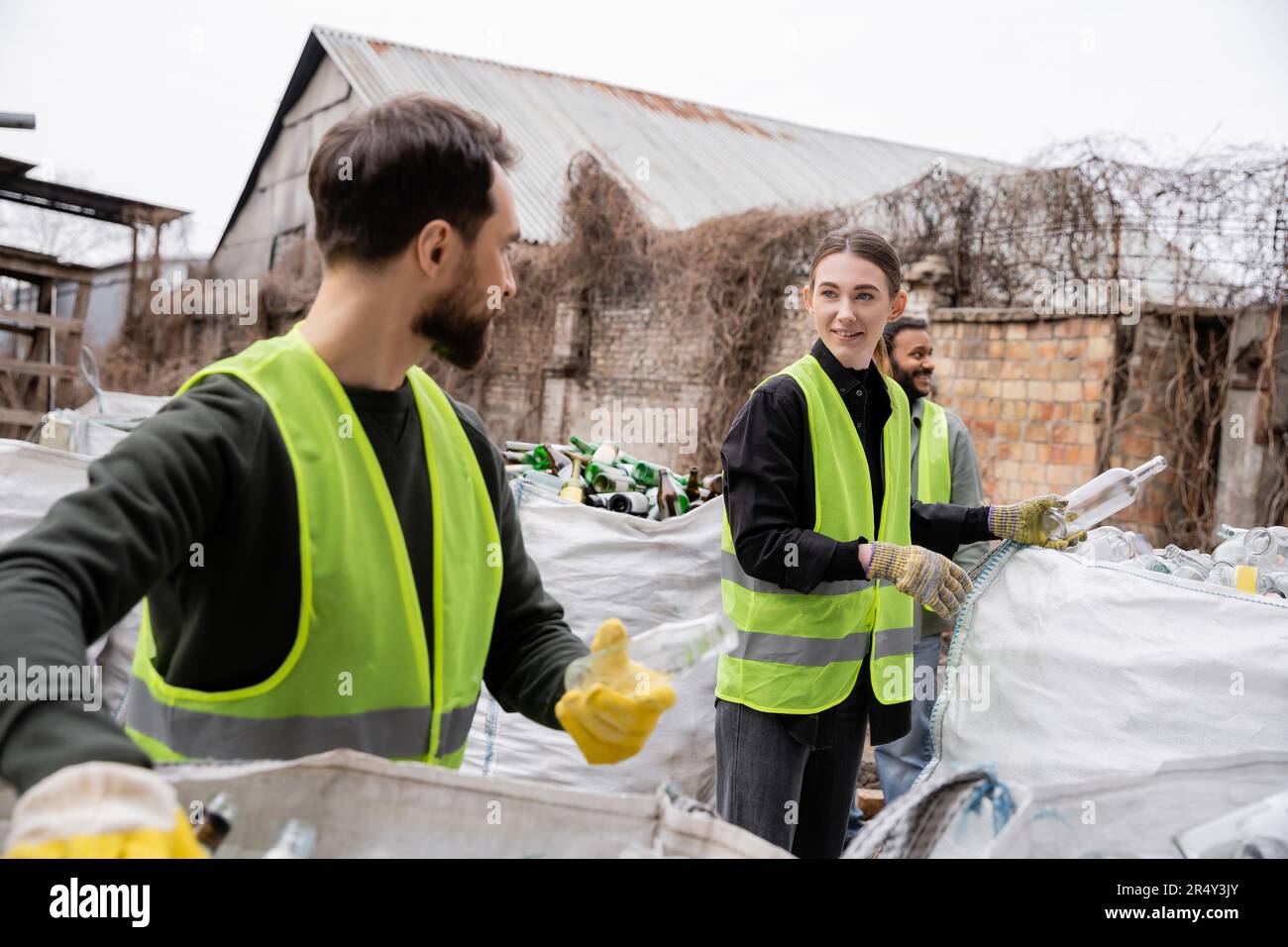 Smiling worker in safety vest and gloves holding glass trash near ...