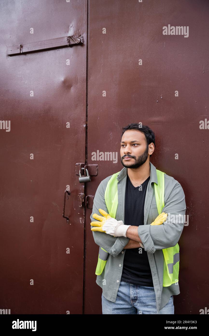 Bearded indian worker in high visibility vest and gloves crossing arms ...