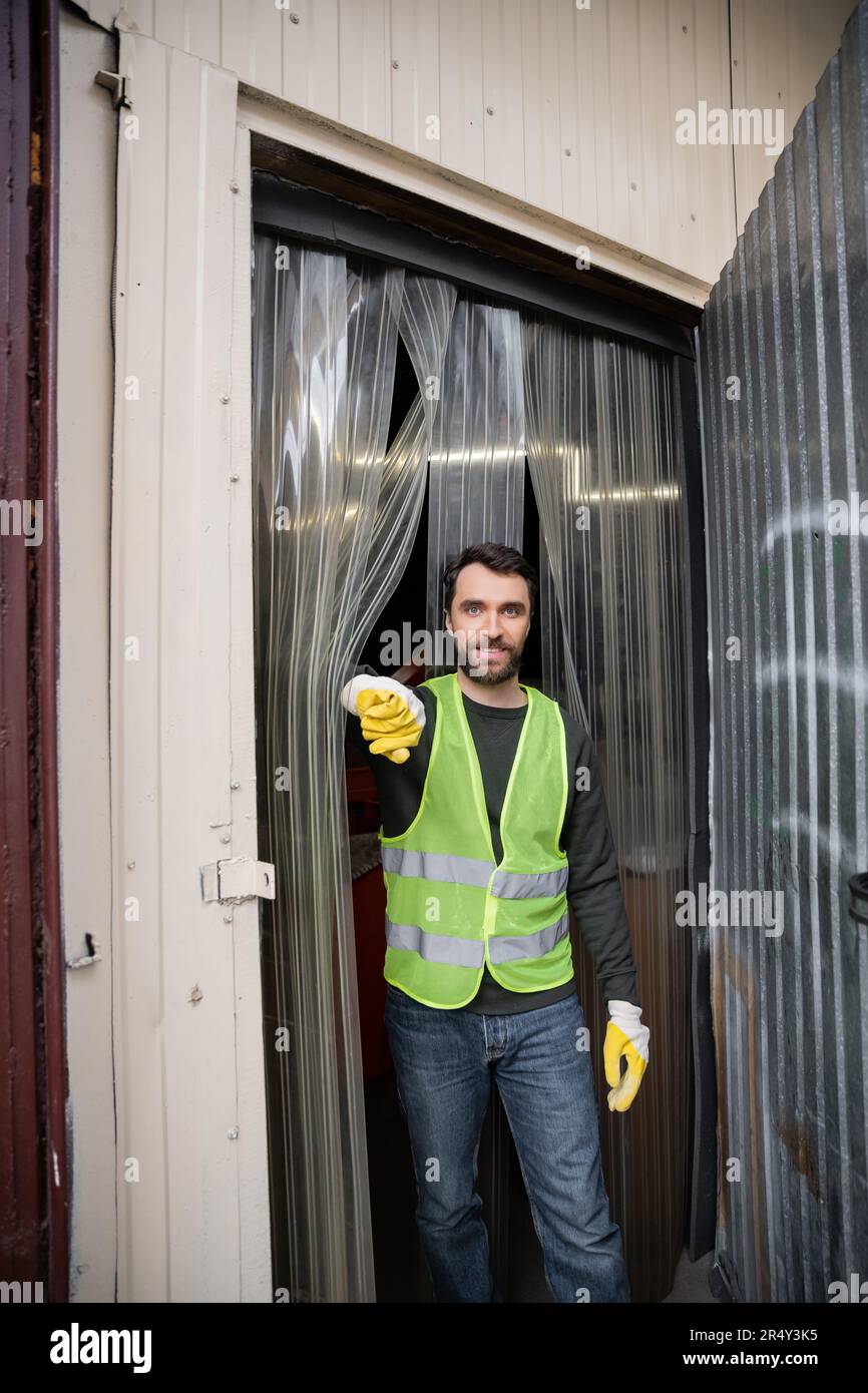 Cheerful male worker in fluorescent vest and protective gloves looking ...