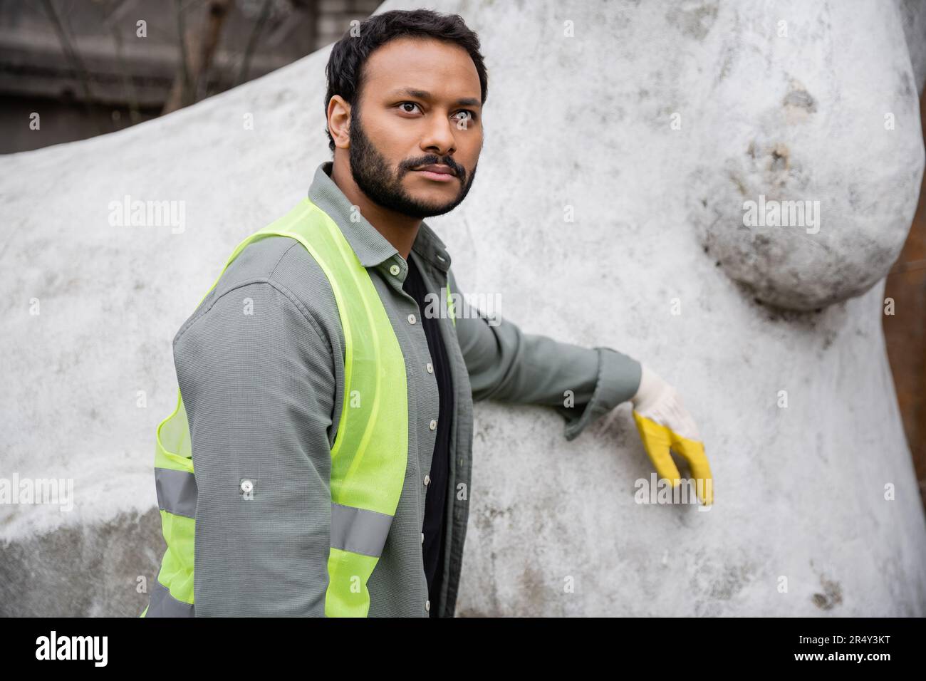 Serious indian worker in high visibility vest and glove standing near ...