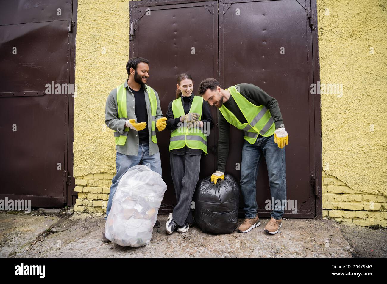 Cheerful worker in high visibility vest and gloves putting trash bag ...