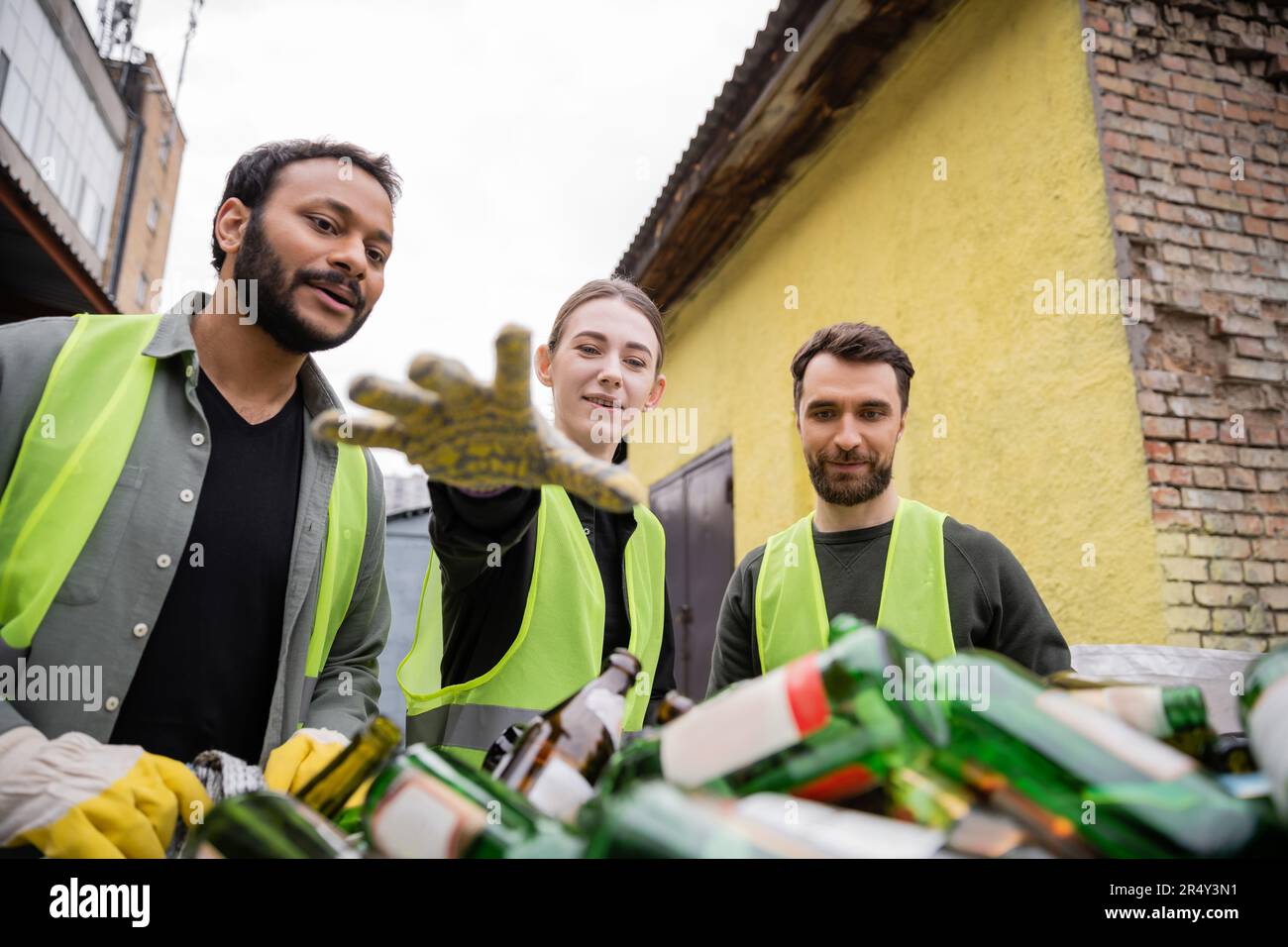Smiling multiethnic workers in gloves and protective vests looking at ...