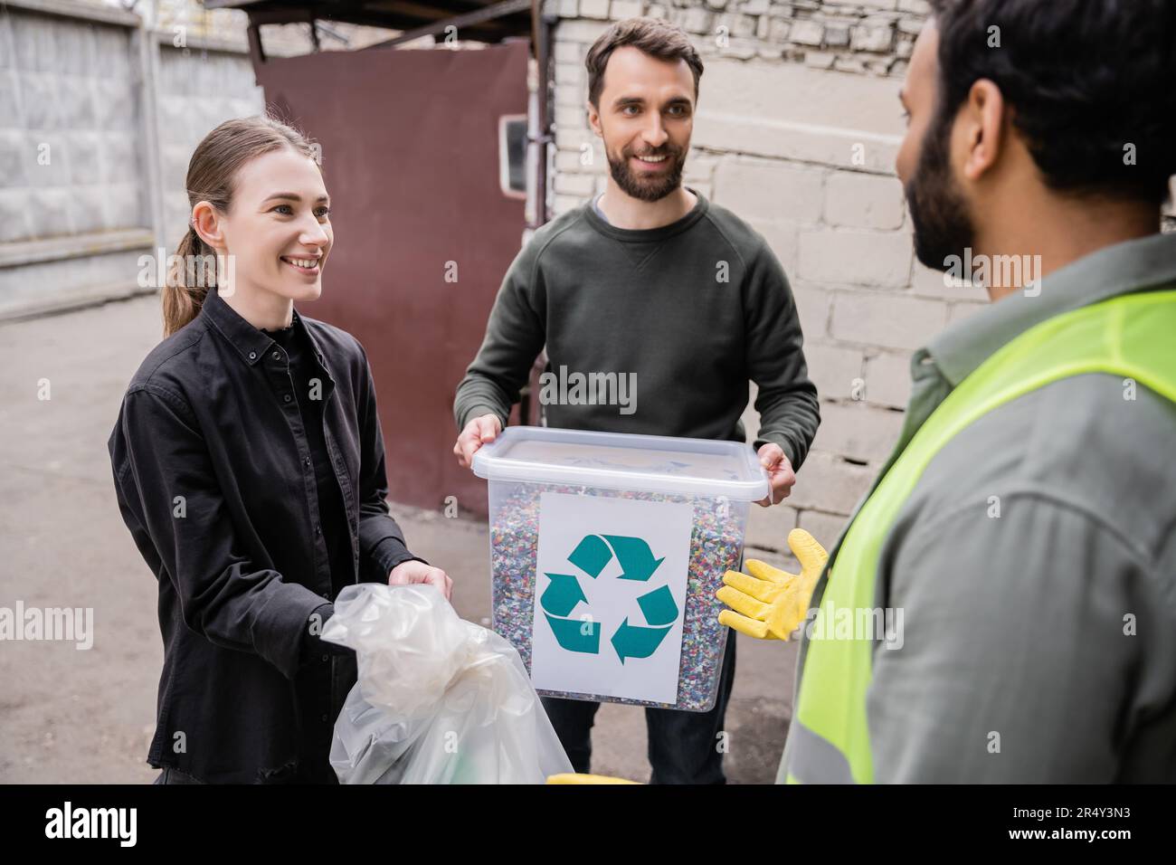 Smiling volunteers holding waste near blurred indian worker in safety ...