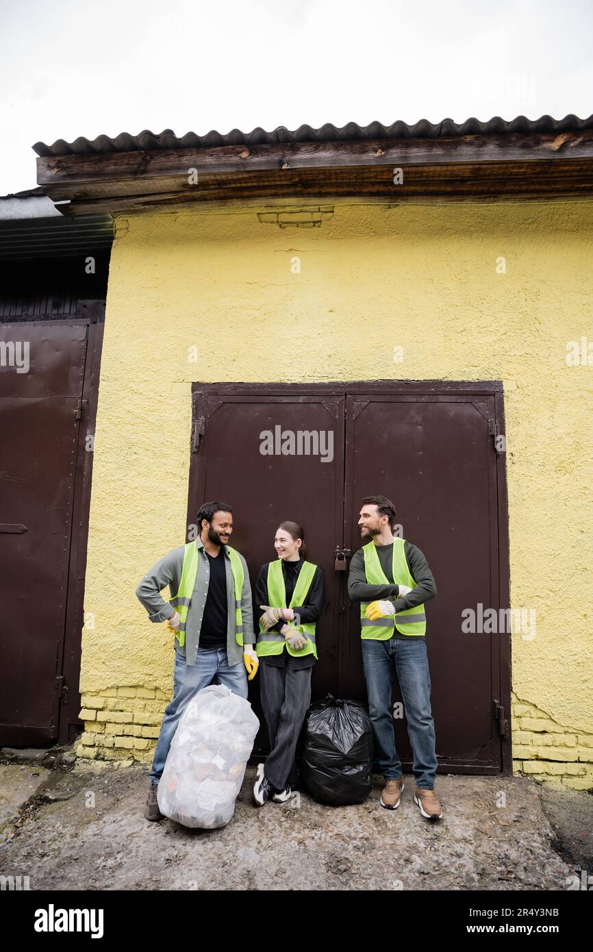 Positive multiethnic workers in safety vests and gloves talking while ...