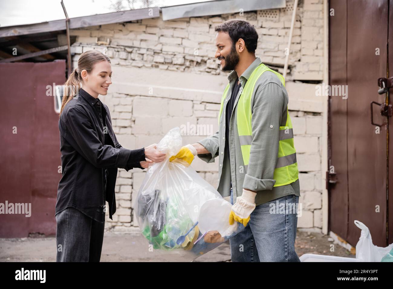 Positive indian worker in safety vest and gloves taking plastic bag ...