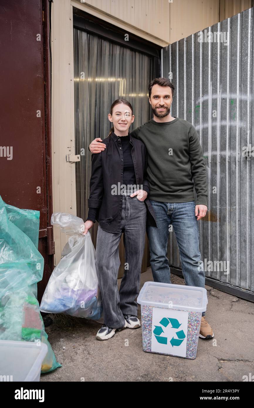 Smiling volunteers looking at camera while standing tear trash and door ...