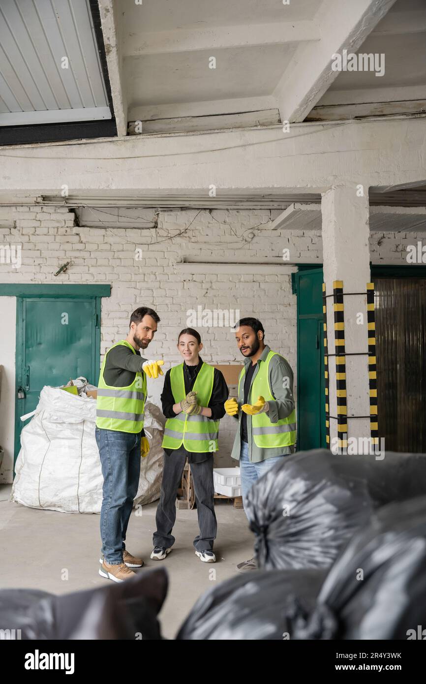 Bearded worker in protective vest and gloves pointing with finger at ...