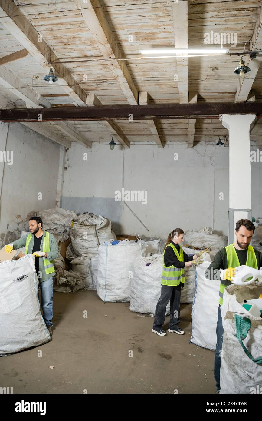 Interracial workers in high visibility vests and gloves soring trash in ...