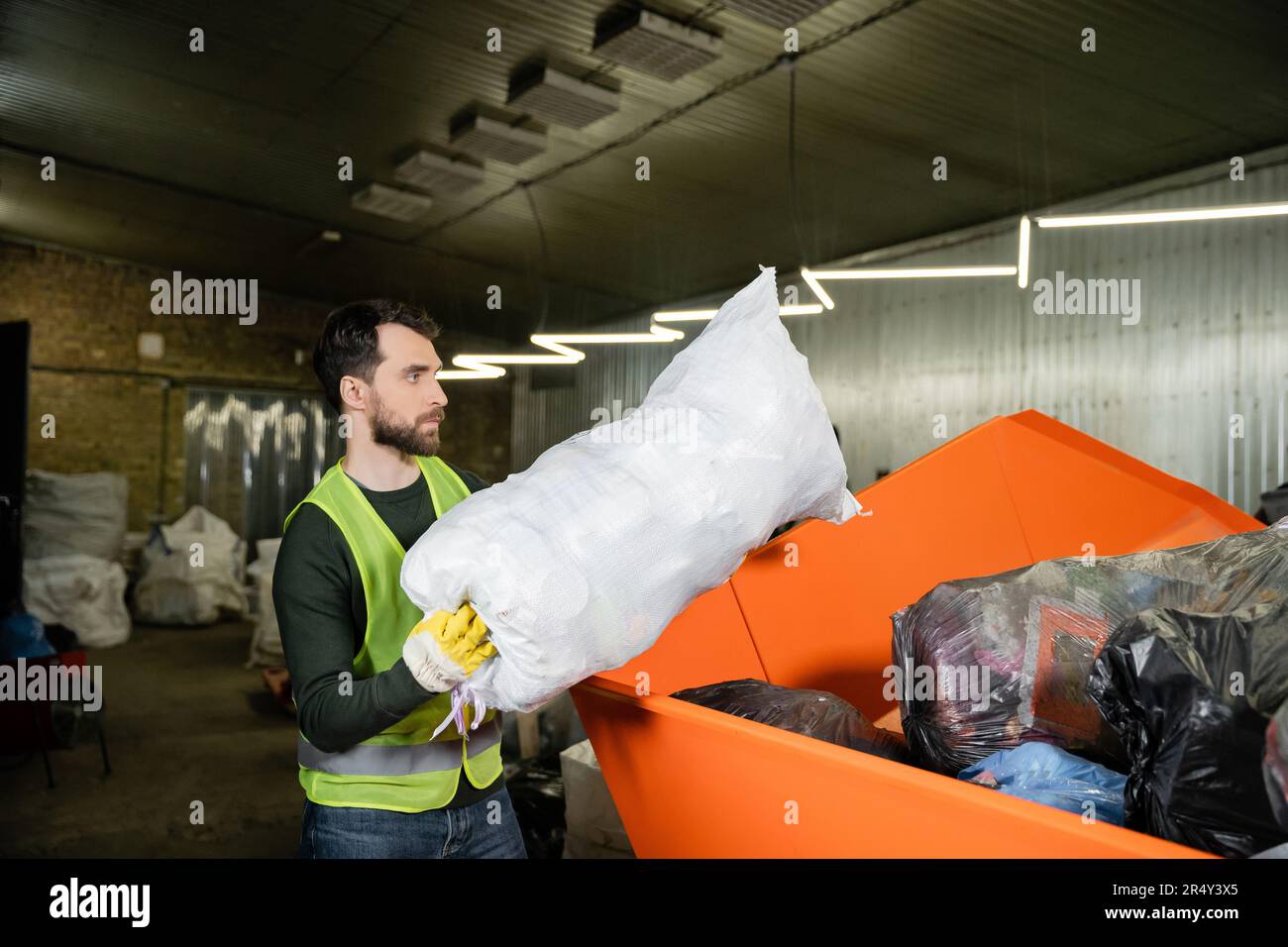 Side view of man in high visibility vest and glove putting sack with ...