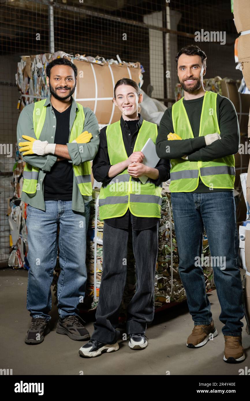 Positive worker in protective vest holding digital tablet and standing ...