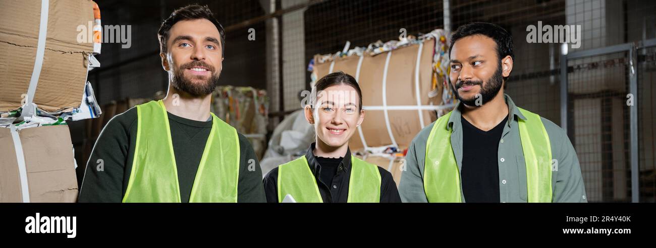 Cheerful and interracial workers in high visibility vests looking at ...