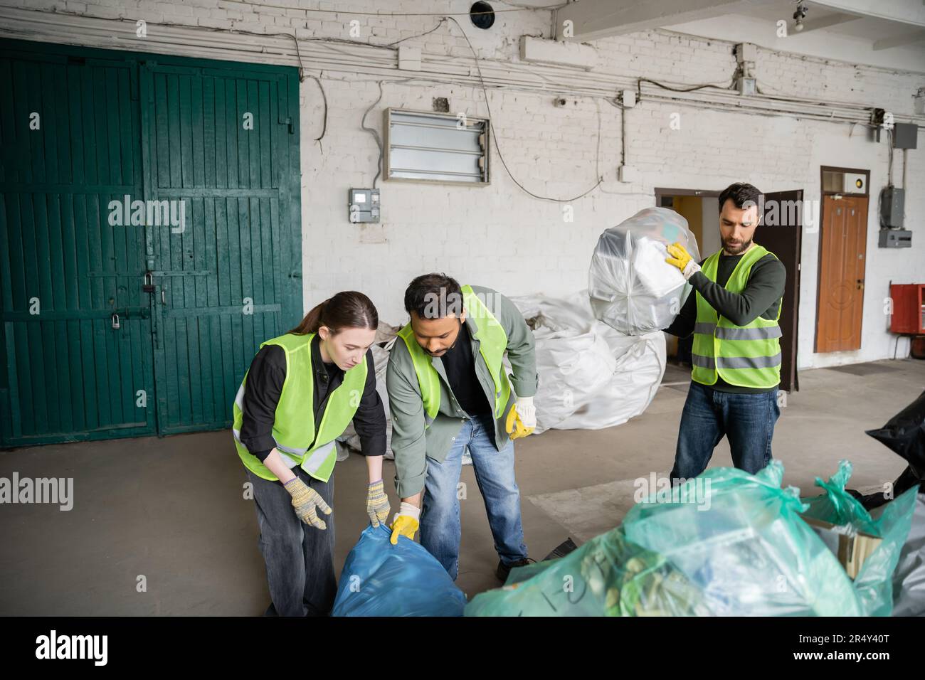 Multiethnic workers in protective vests and gloves working with plastic ...