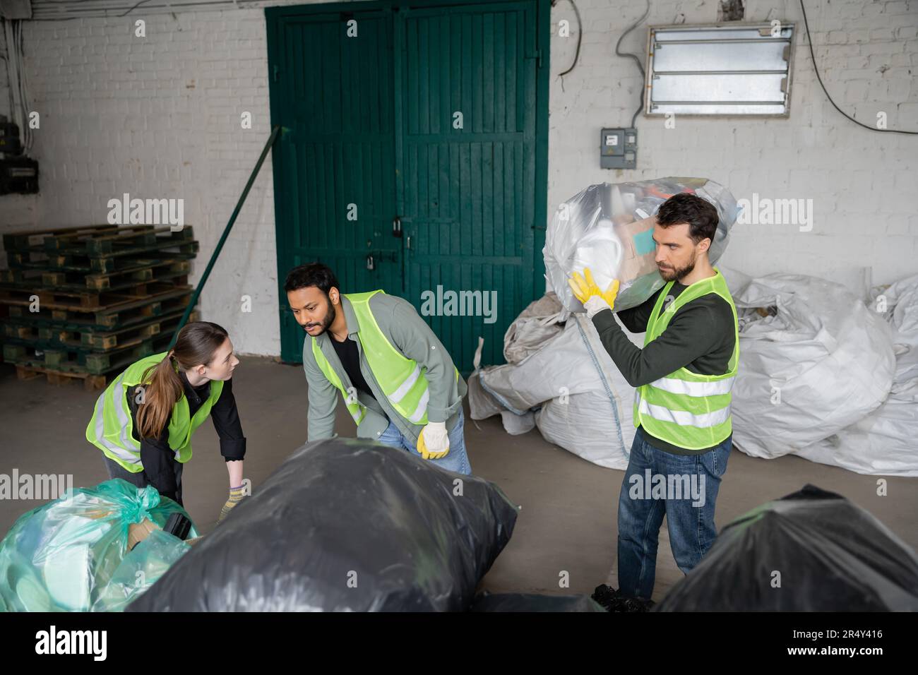 Multiethnic workers in high visibility vests and gloves working with ...