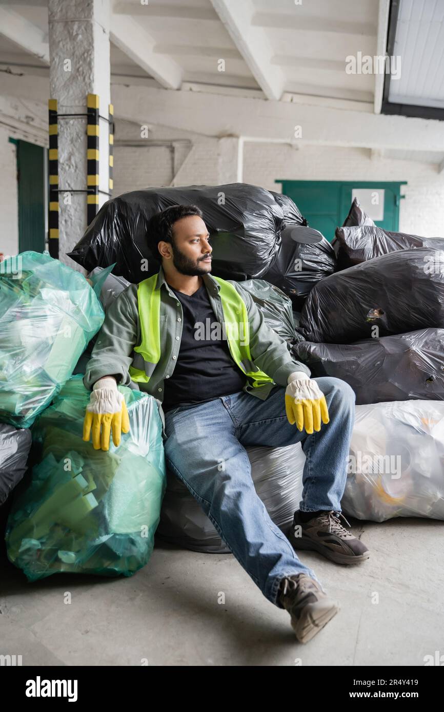 Indian worker in high visibility vest and gloves looking away while ...