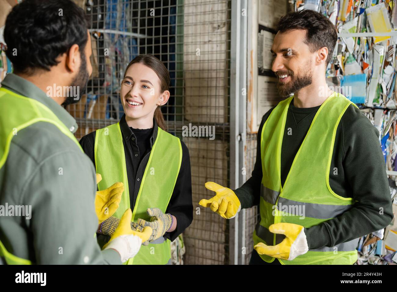 Cheerful man in high visibility vest and gloves talking to multiethnic ...