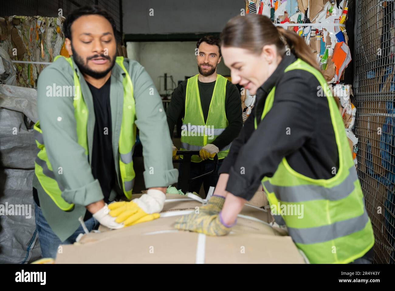 Smiling worker in reflective vest and gloves standing near hand pallet ...