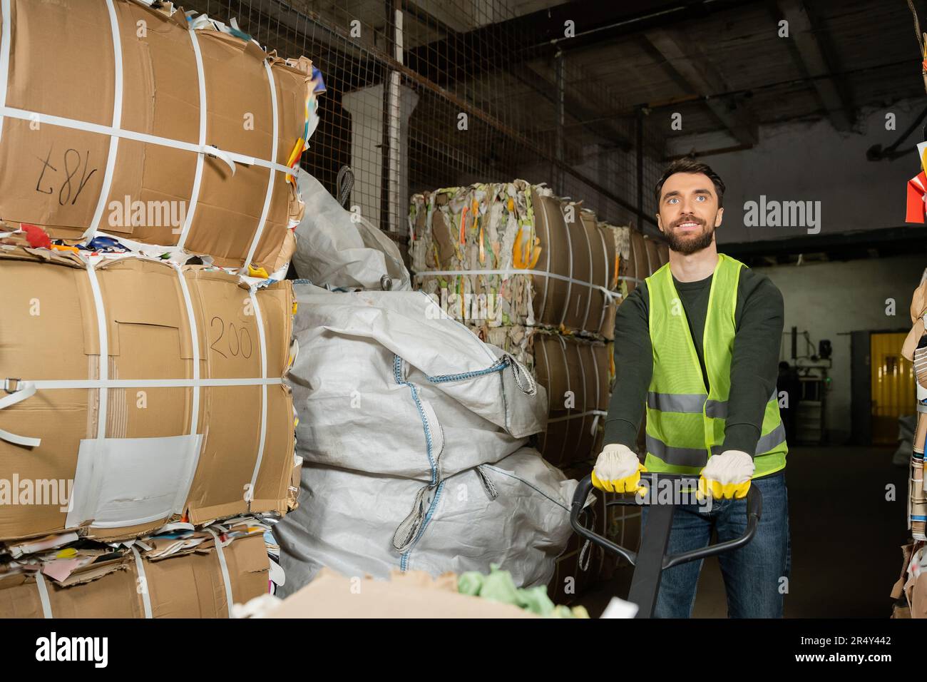 Smiling and bearded worker in reflective vest and gloves using hand ...