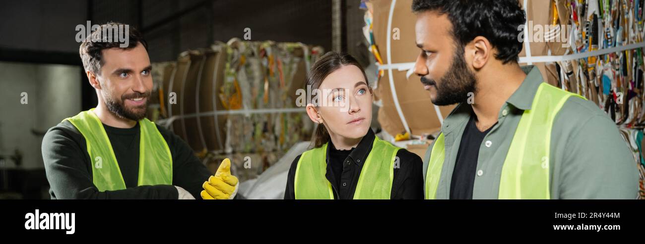 Smiling worker in safety vest and glove talking to indian colleague ...