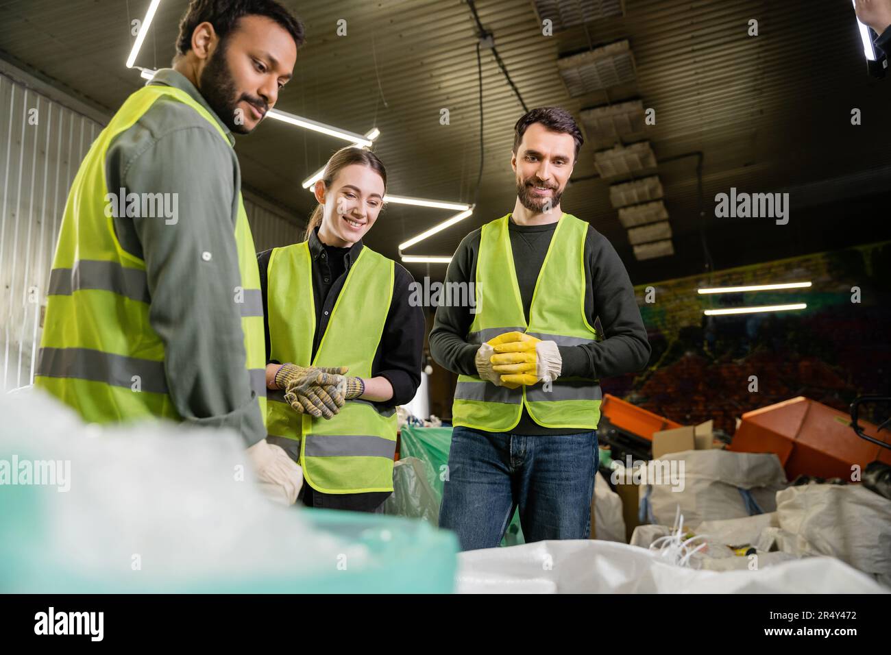 Smiling multiethnic workers in protective vests and gloves looking at ...