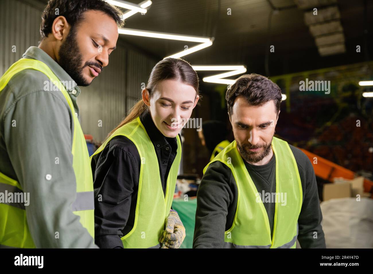 Cheerful workers in high visibility vests looking away while indian ...