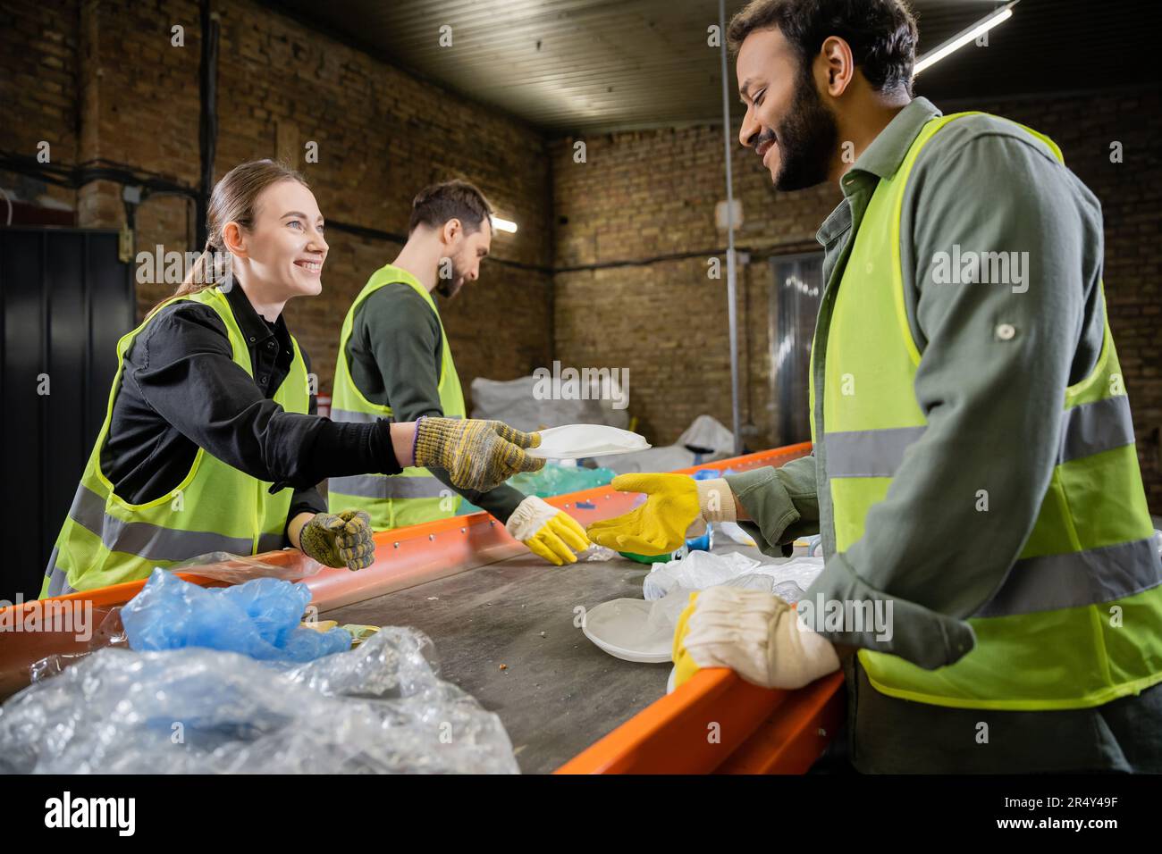 Cheerful sorter in high visibility vest and gloves giving plastic trash ...