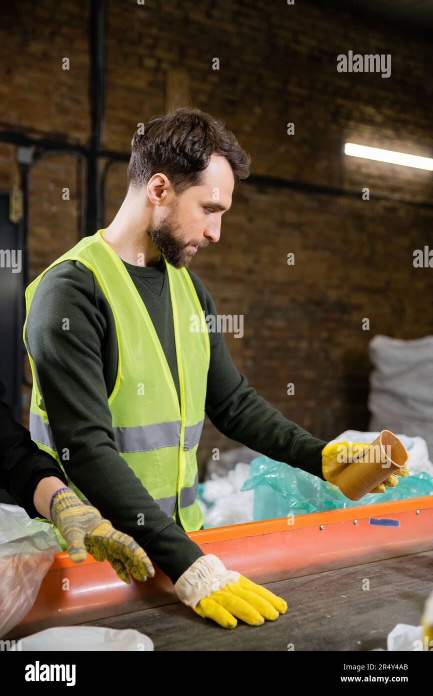 Sorter in reflective vest and protective gloves holding paper cup near ...