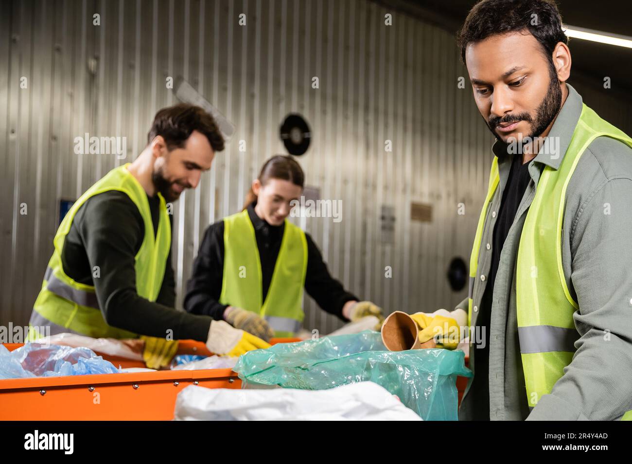 Bearded indian sorter in glove and high visibility vest putting paper ...