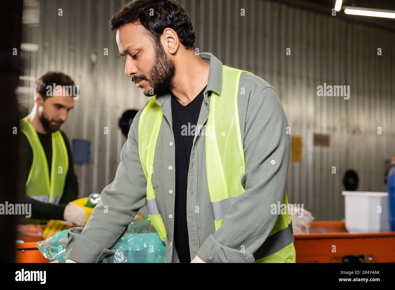 Bearded indian worker in high visibility vest separating trash while ...