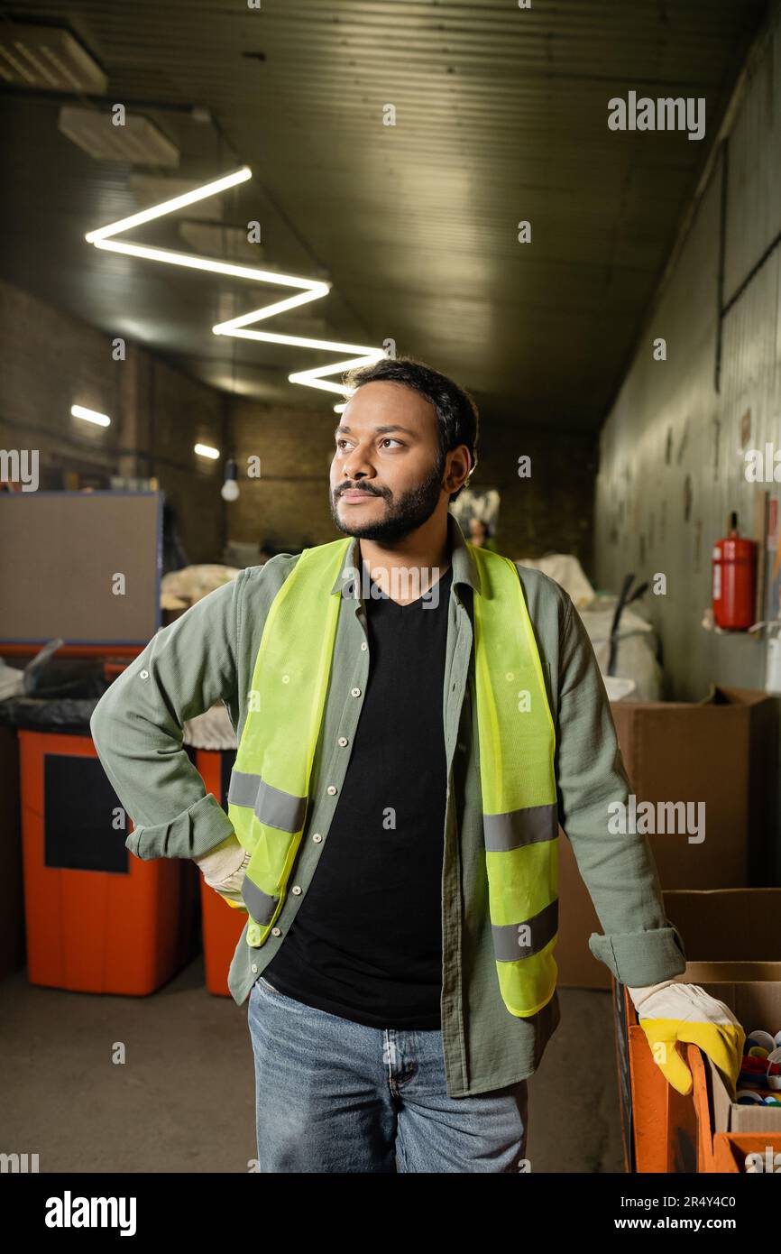 Indian man in high visibility vest and gloves looking away while ...