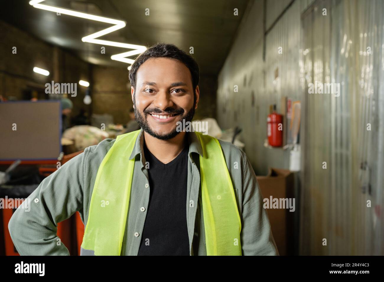 Portrait of cheerful indian sorter in high visibility vest looking at ...