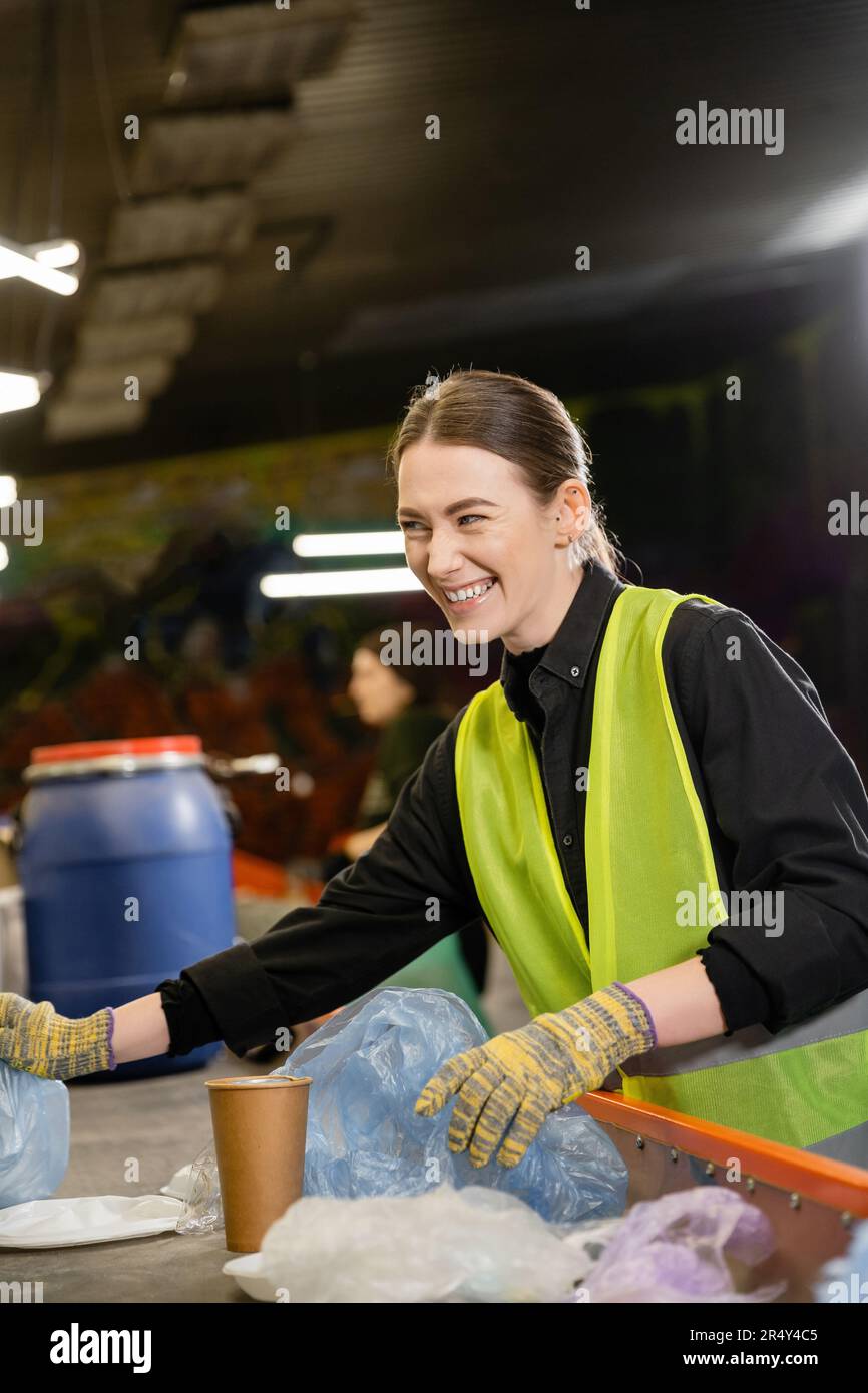Cheerful young worker in protective vest and gloves sorting garbage on ...