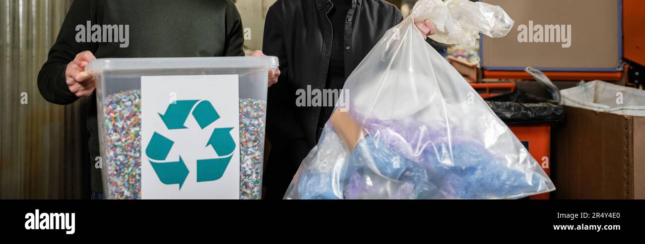 Cropped view of volunteers holding trash bin with recycle sign and bag ...
