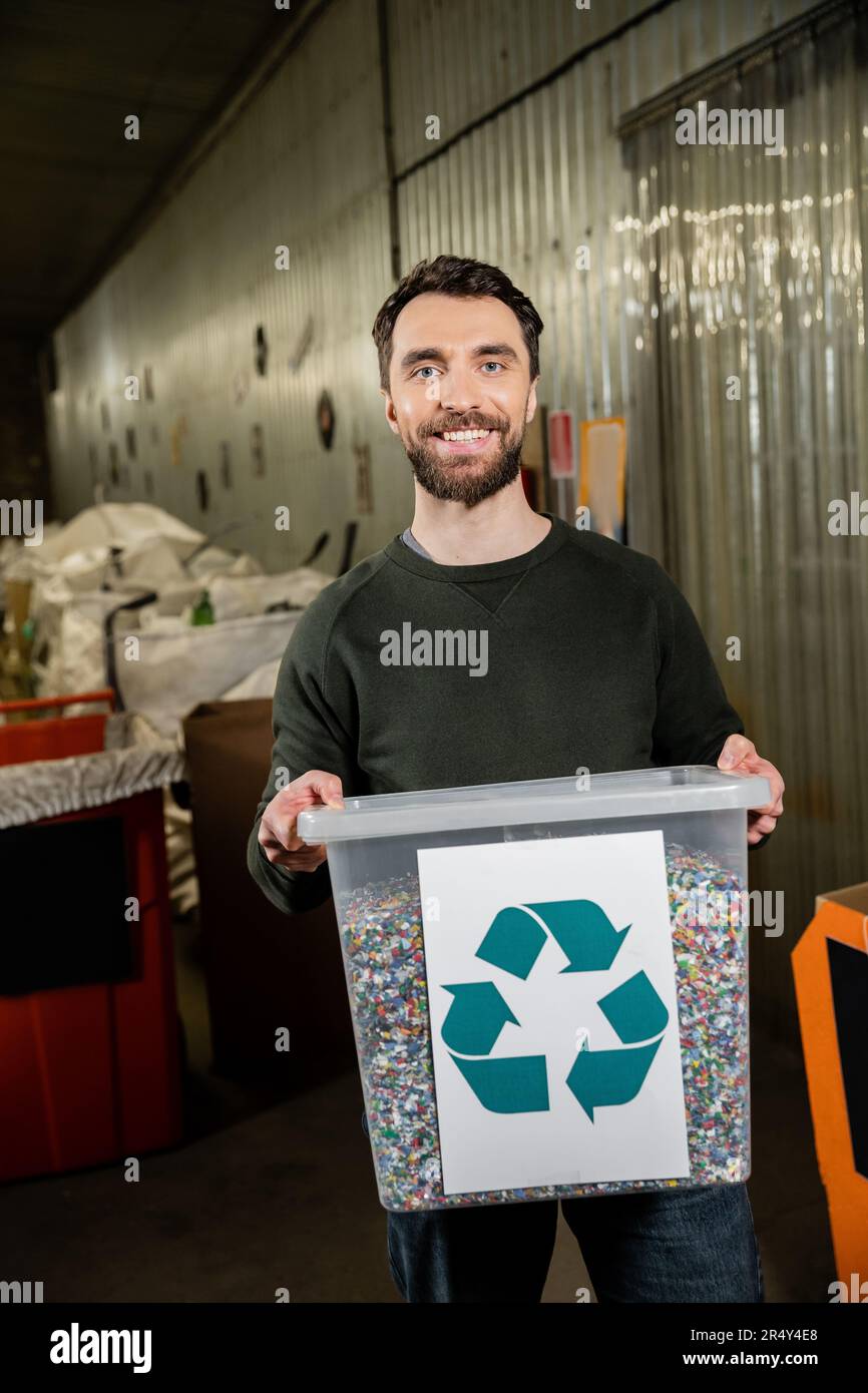 Cheerful and bearded volunteer looking at camera while holding trash ...