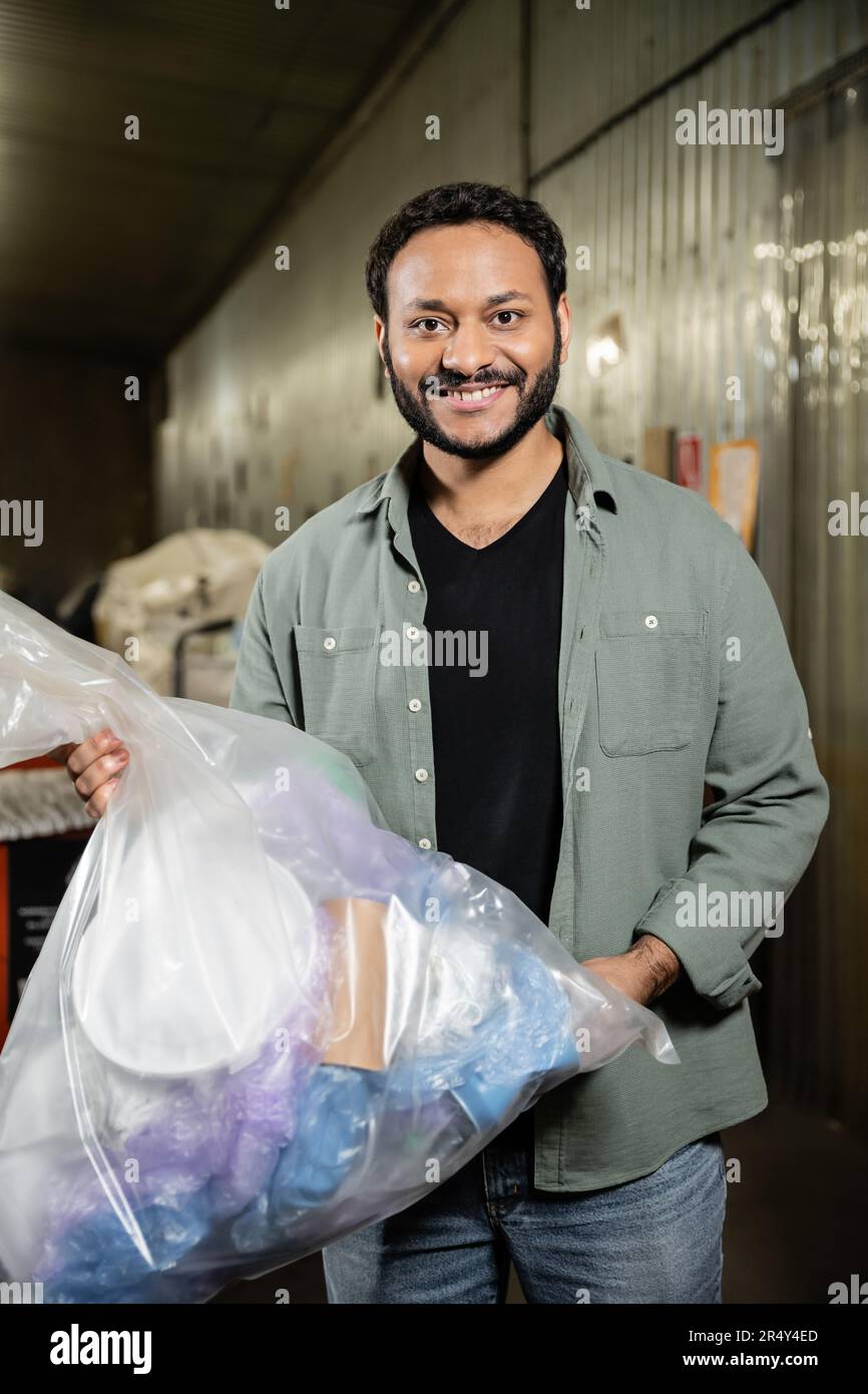 Smiling indian volunteer looking at camera while holding plastic bag ...