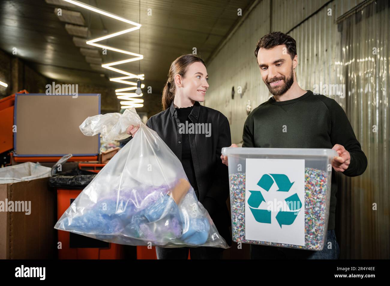 Smiling volunteer holding trash bag near man with bin and recycle sign ...