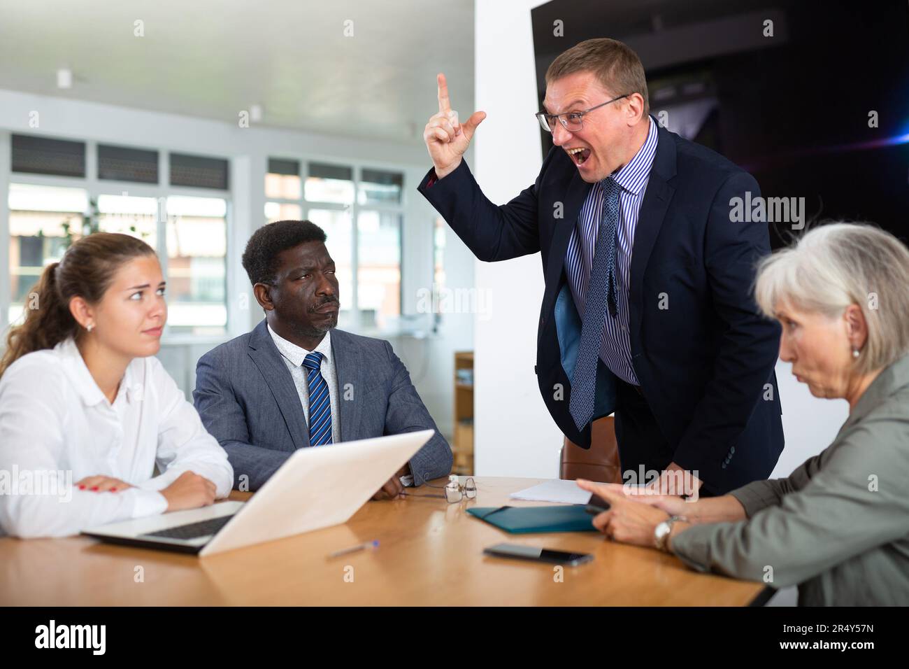 Angry middle-aged man shouting at his business partners sitting around ...