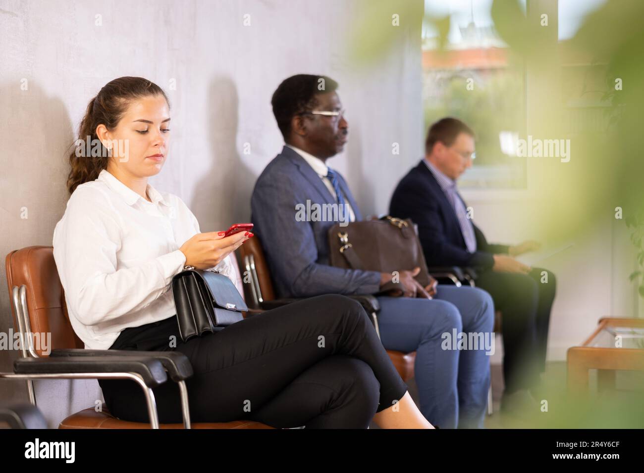 Young woman sitting in line at reception with phone Stock Photo - Alamy
