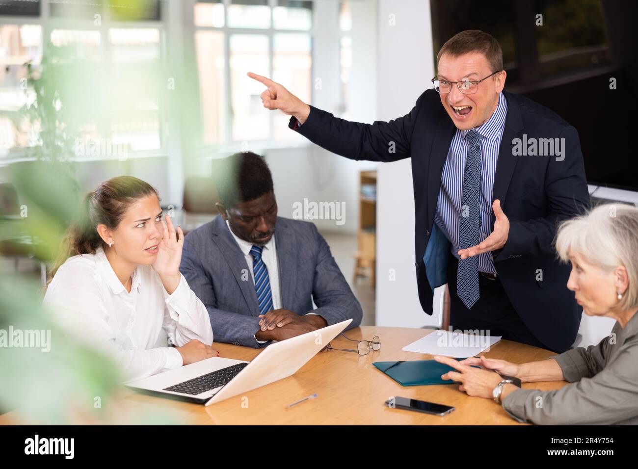 Angry middle-aged man shouting at his business partners sitting around ...