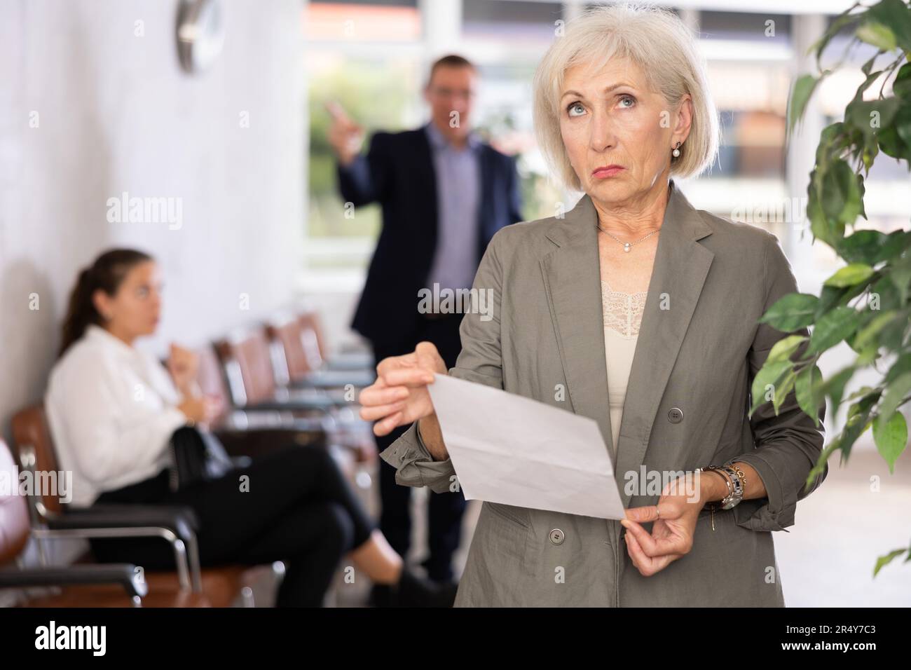 Upset old woman standing in waiting room with her back to person who is ...