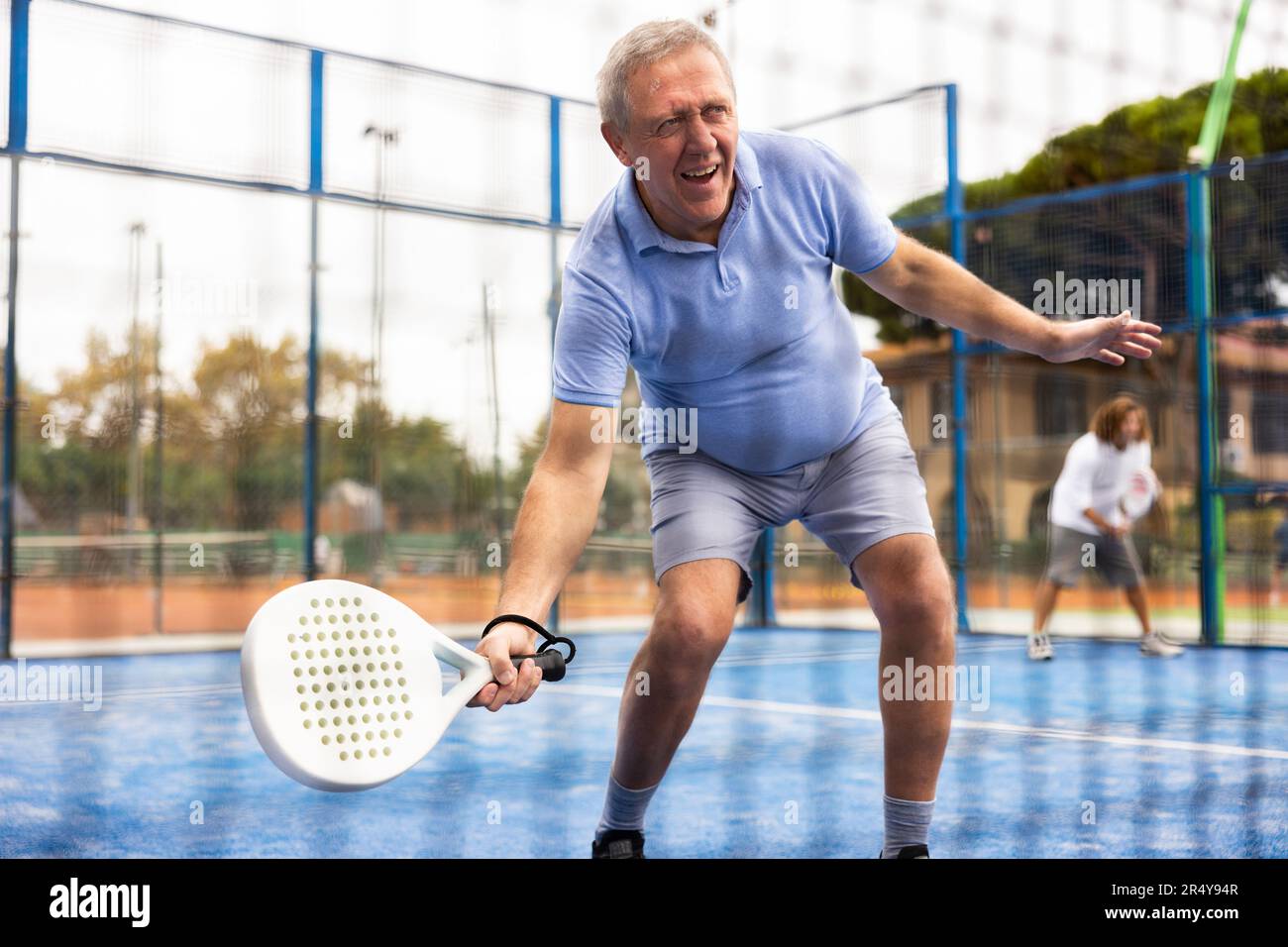 European old man holding playing padel during training in court. View ...