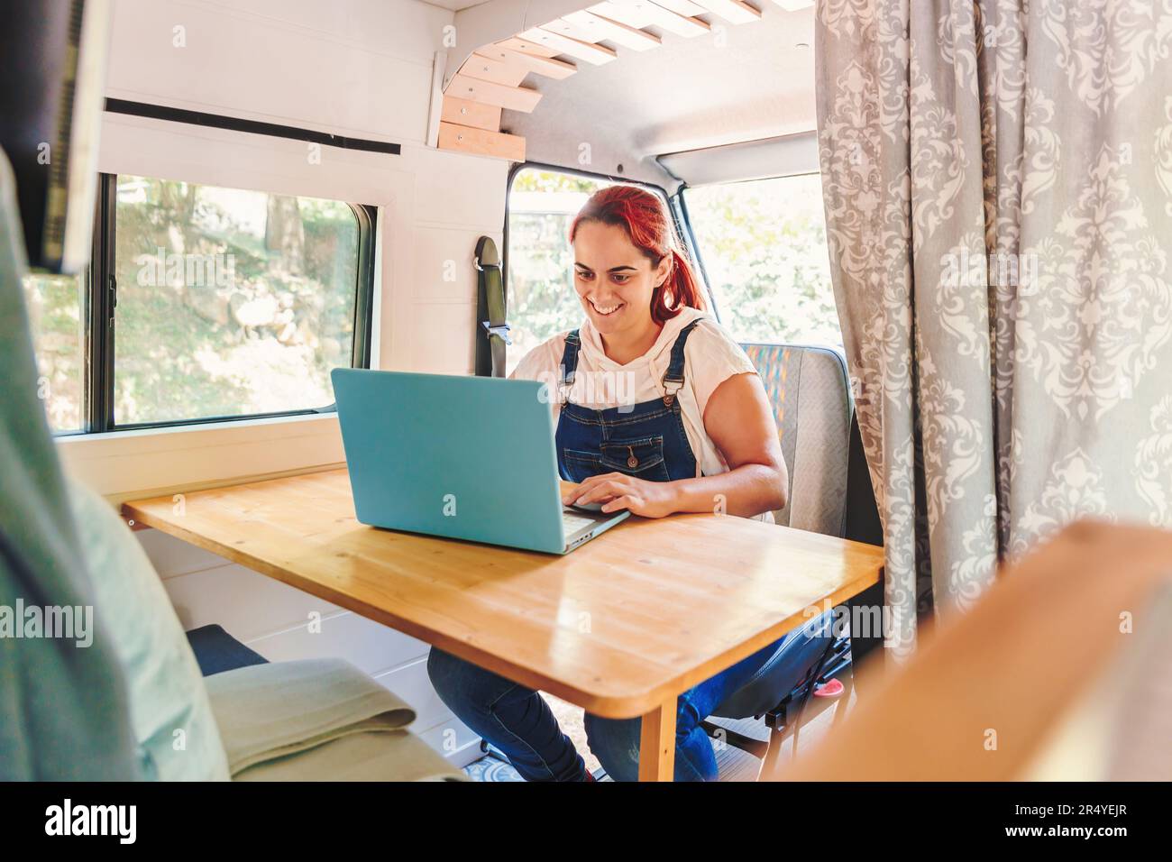 Caucasian young woman working on her laptop in her handmade camper van ...