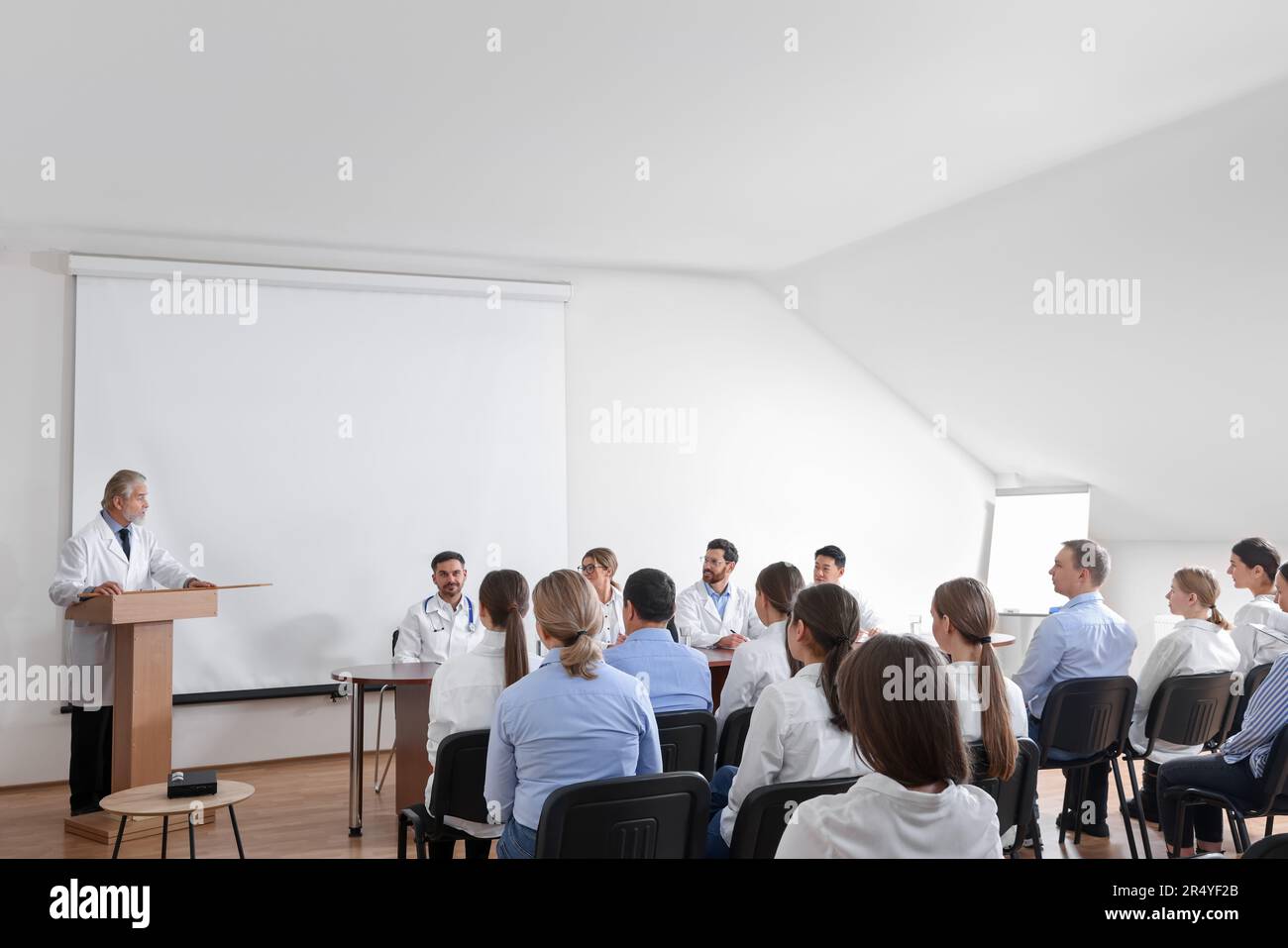 Senior doctor giving lecture in conference room with projection screen ...