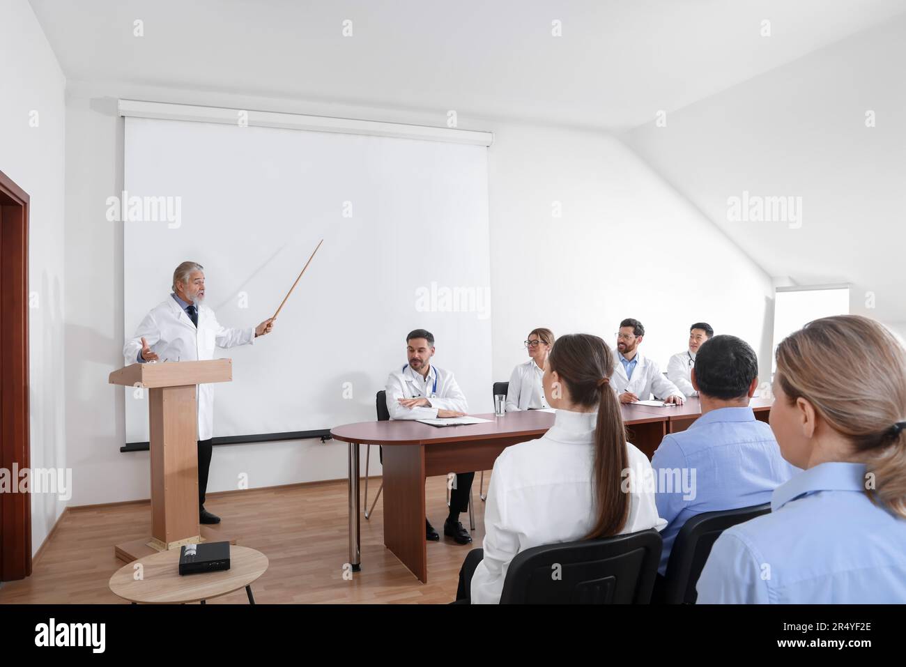 Senior doctor giving lecture in conference room with projection screen ...
