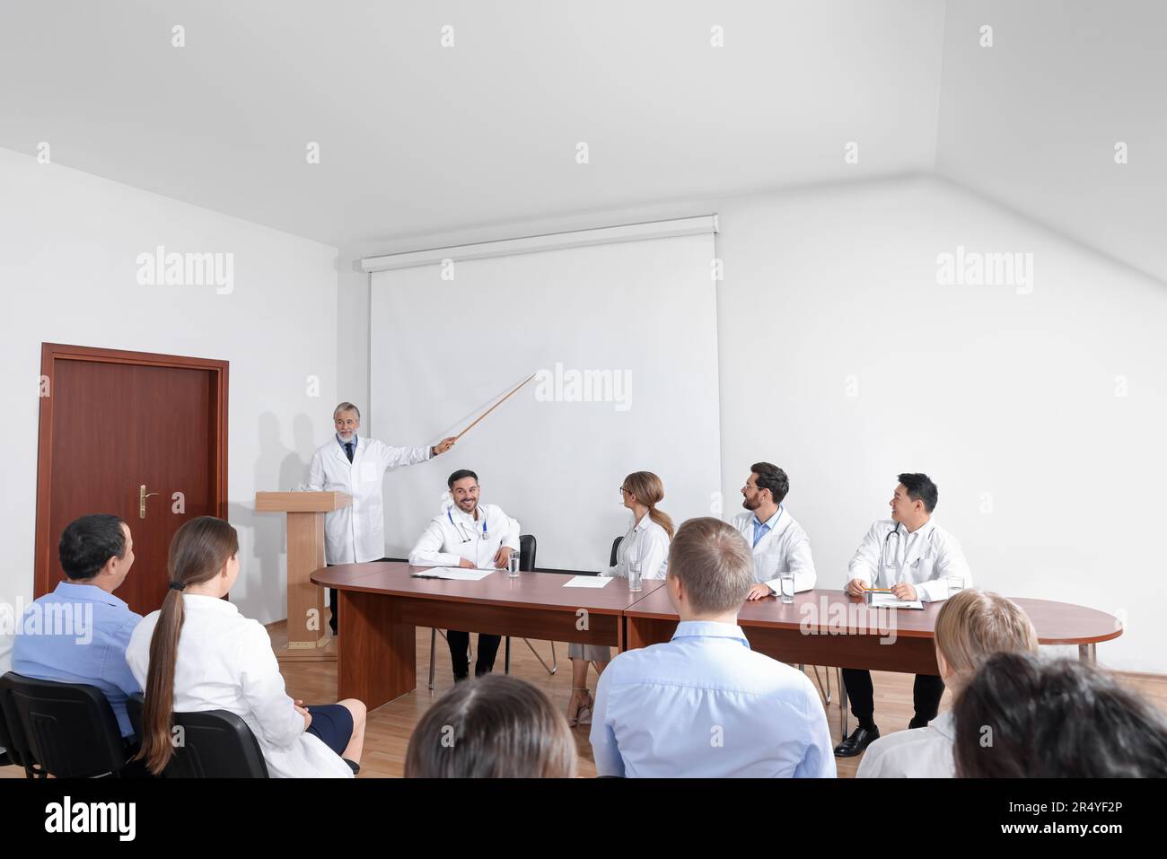 Senior doctor giving lecture in conference room with projection screen ...