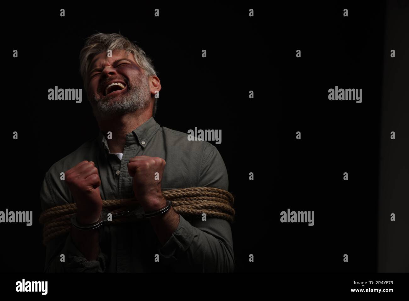 Emotional beaten man tied with rope on black background, space for text ...