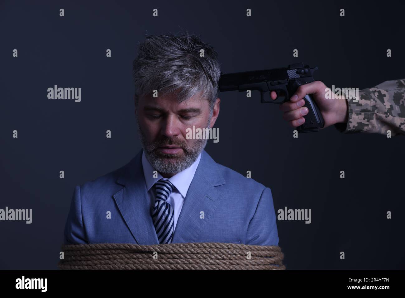 Kidnapper aiming gun at tied victim on dark background. Hostage taking ...